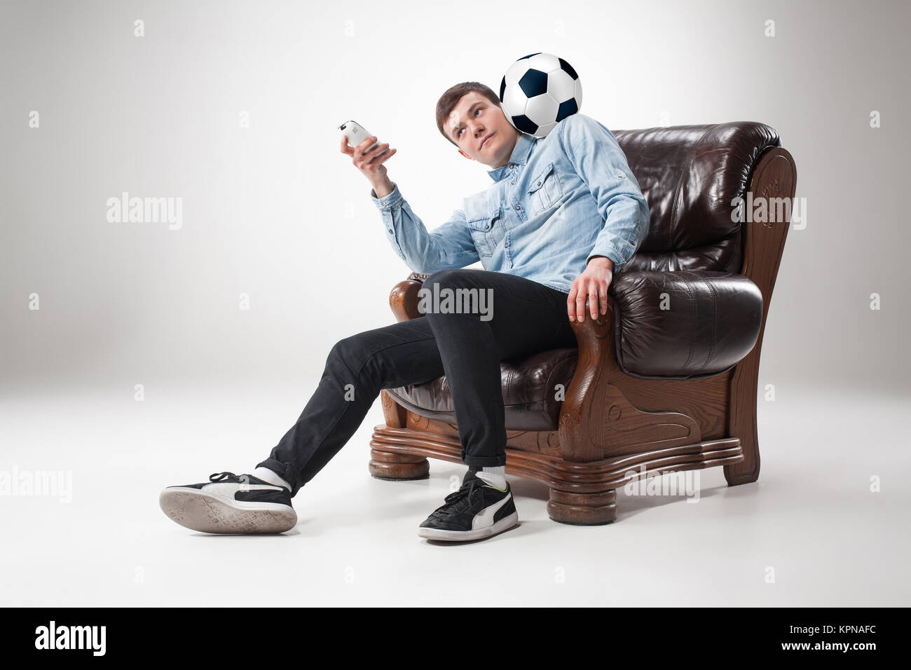 The portrait of fan with ball, holding tv remote on white background ...