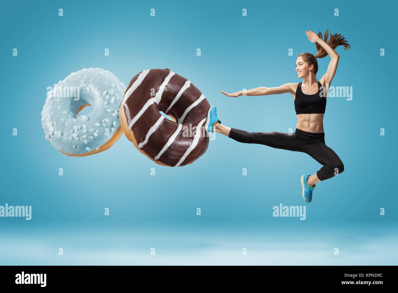 Fit young woman fighting off bad food on a blue background Stock Photo ...
