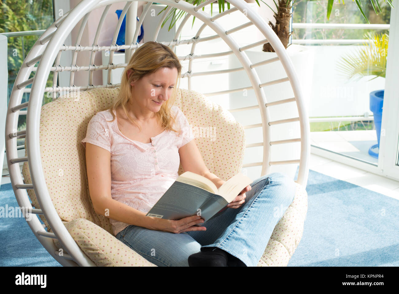 blond woman sitting in chair and reading a book Stock Photo - Alamy