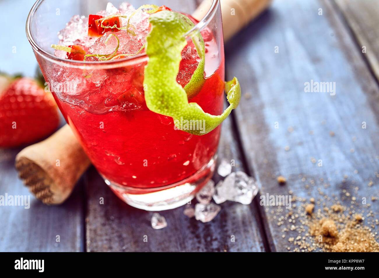 Red zesty strawberry ice slush drink in glass with lime peel and ...