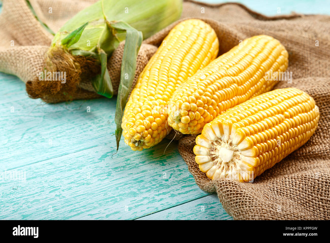 three raw corn in a clay plate on a blue background on a napkin, with ...