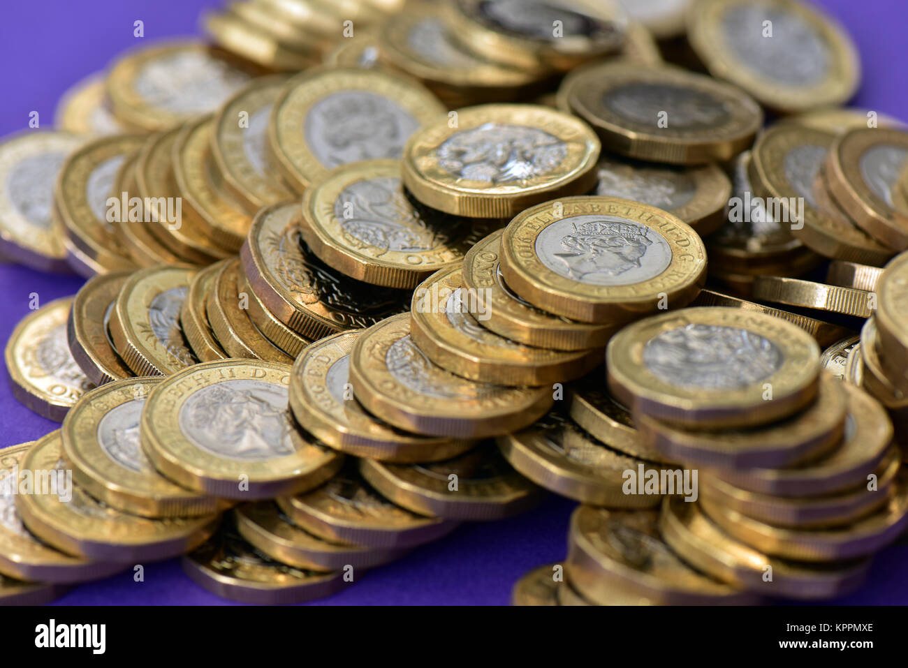 a pile of one pound coins on a purple or regal background. A number of ...