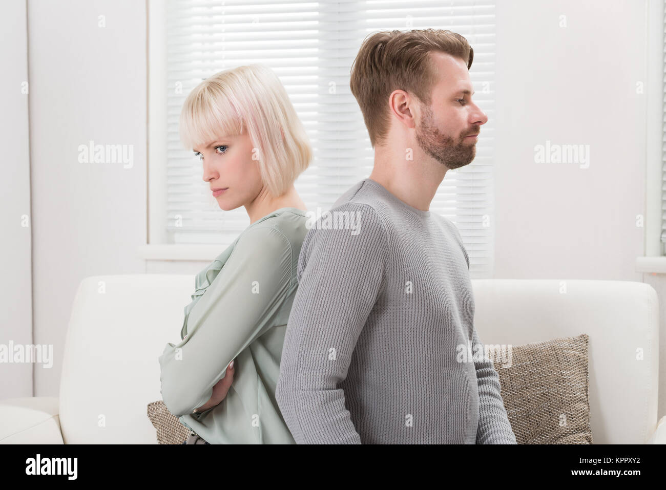 Couple Sitting Back To Back On Couch Stock Photo - Alamy