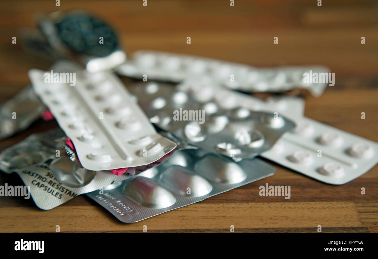 A pile of part used prescription drugs on a tabletop with a watch in ...