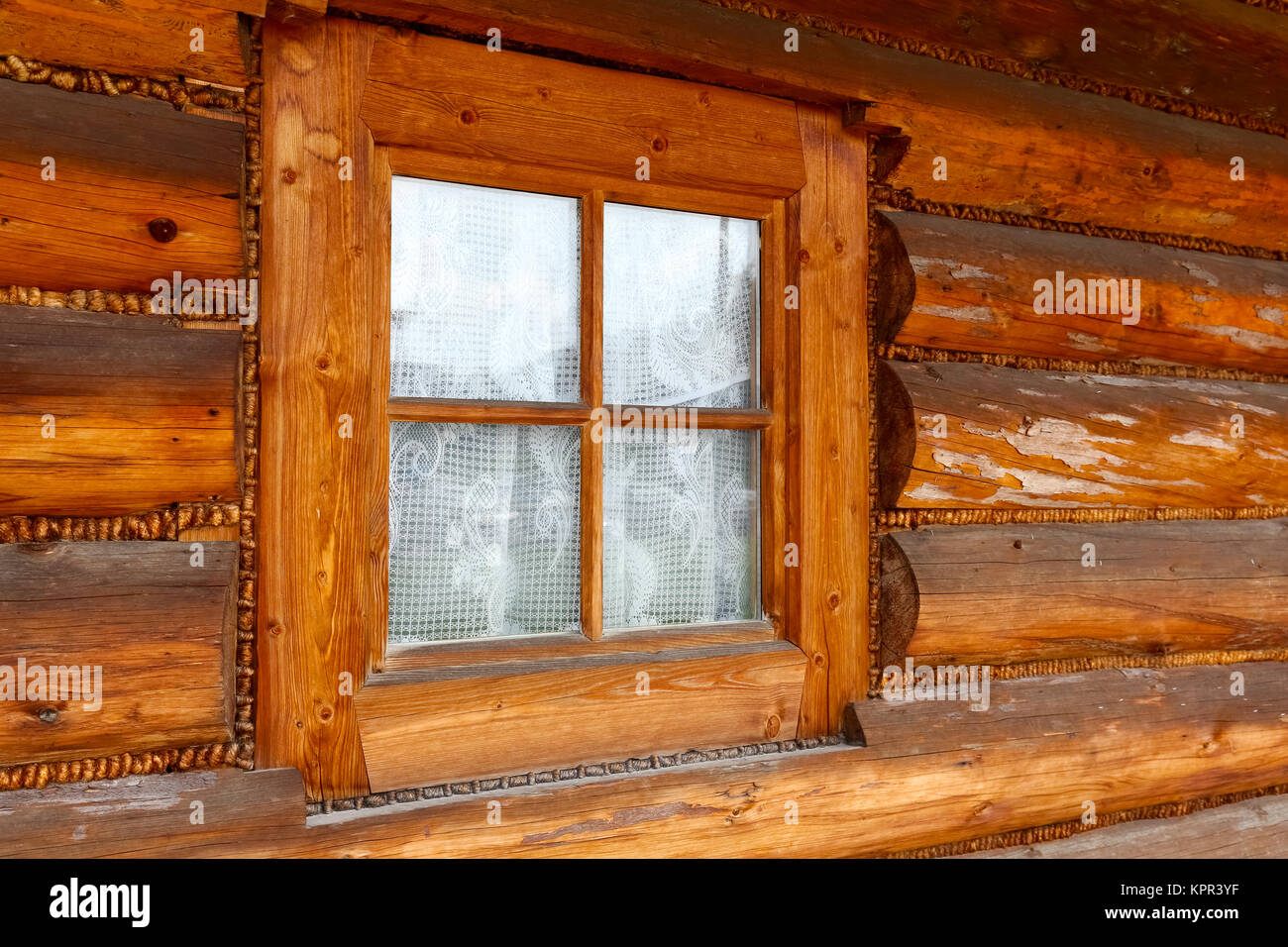 In the wall made of wooden logs, there is a small window in the wooden ...