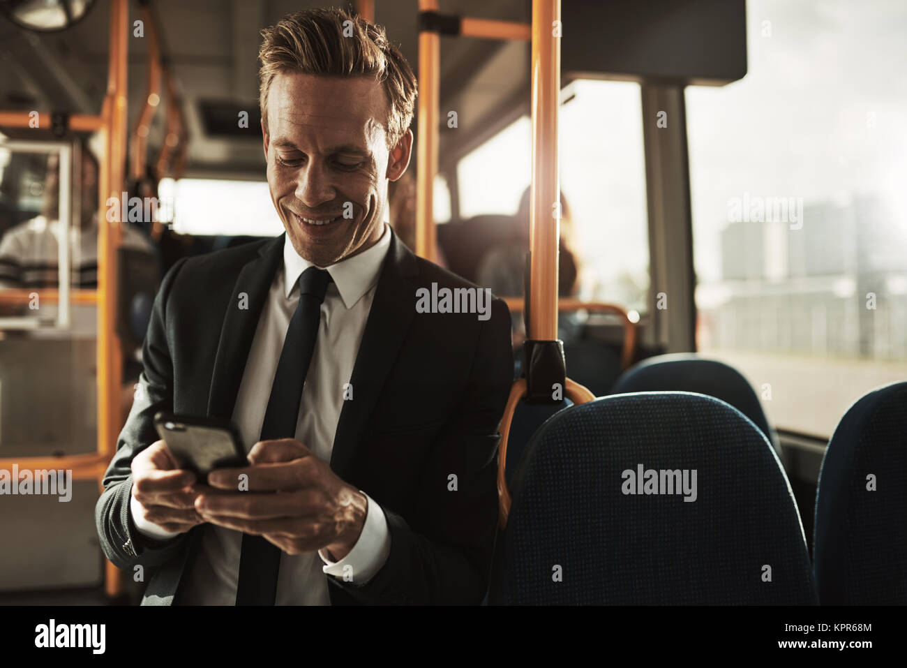 Smiling young businessman wearing a suit standing on a bus during his ...