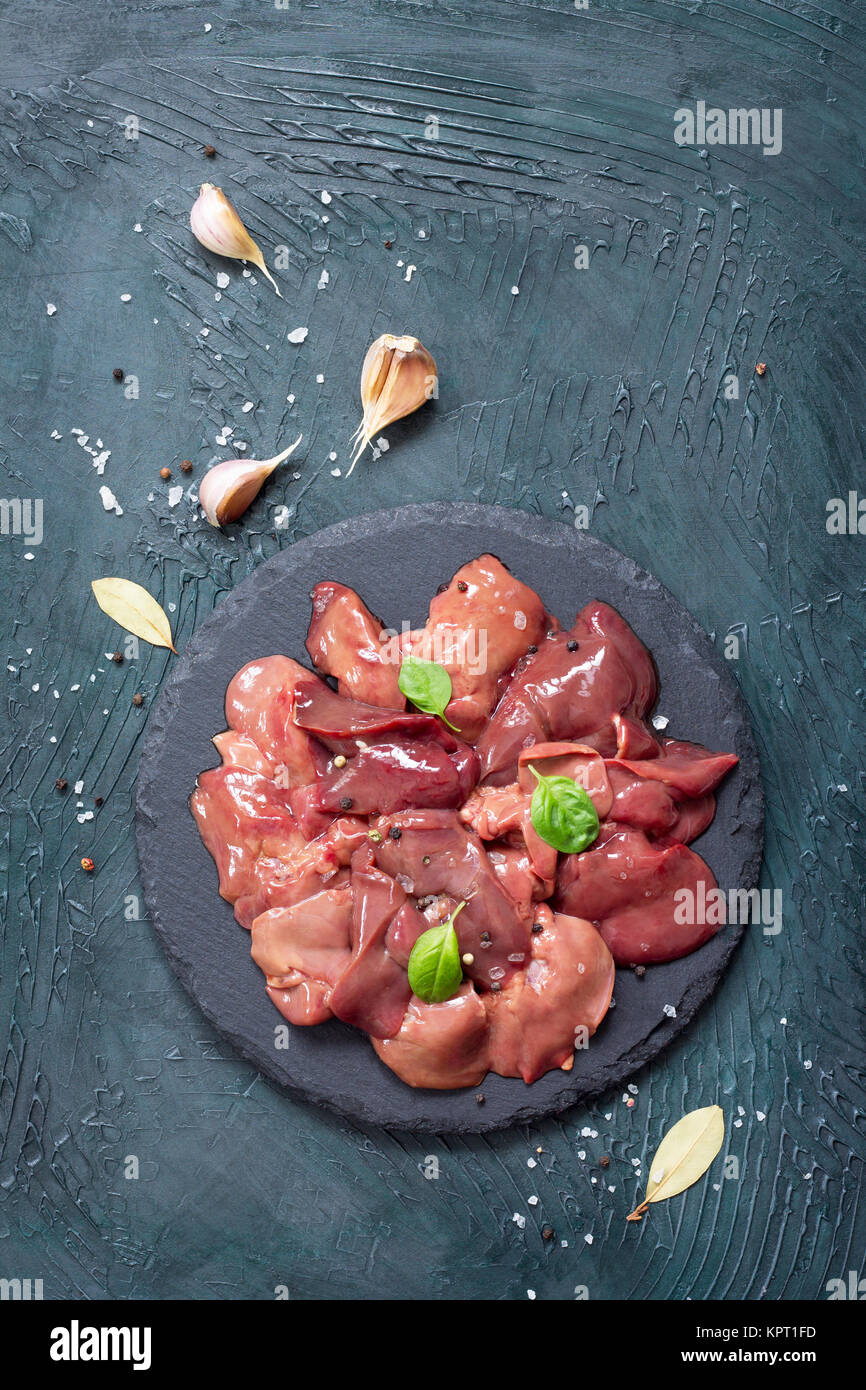 Raw chicken liver on a slate board and spices on a stone with a gray ...