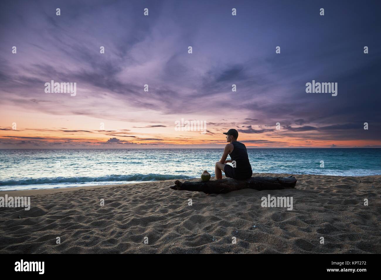 Pensive young man with coconut drink relaxing on the beach during ...