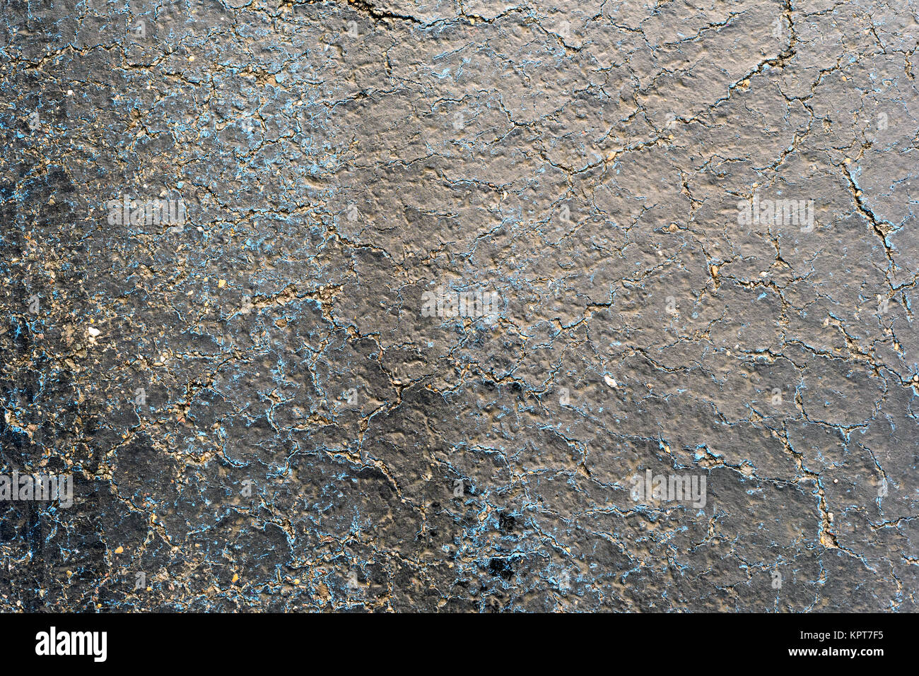 Aged cracked black bitumen tar surface with blue highlights. Copy space ...