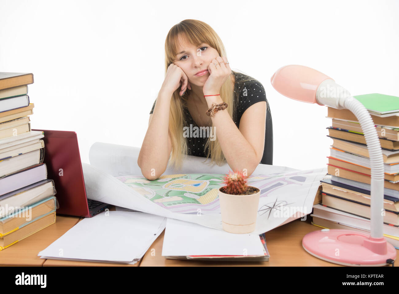 The girl is sad student sitting at a table crammed with books, drawings ...