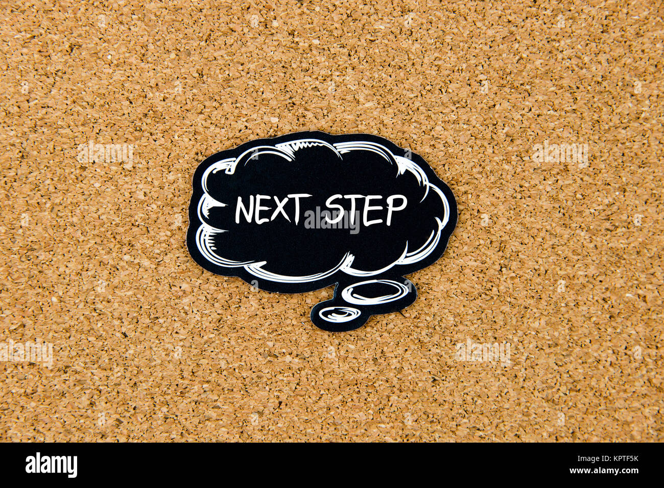 NEXT STEP written on black thinking bubble over cork board background ...