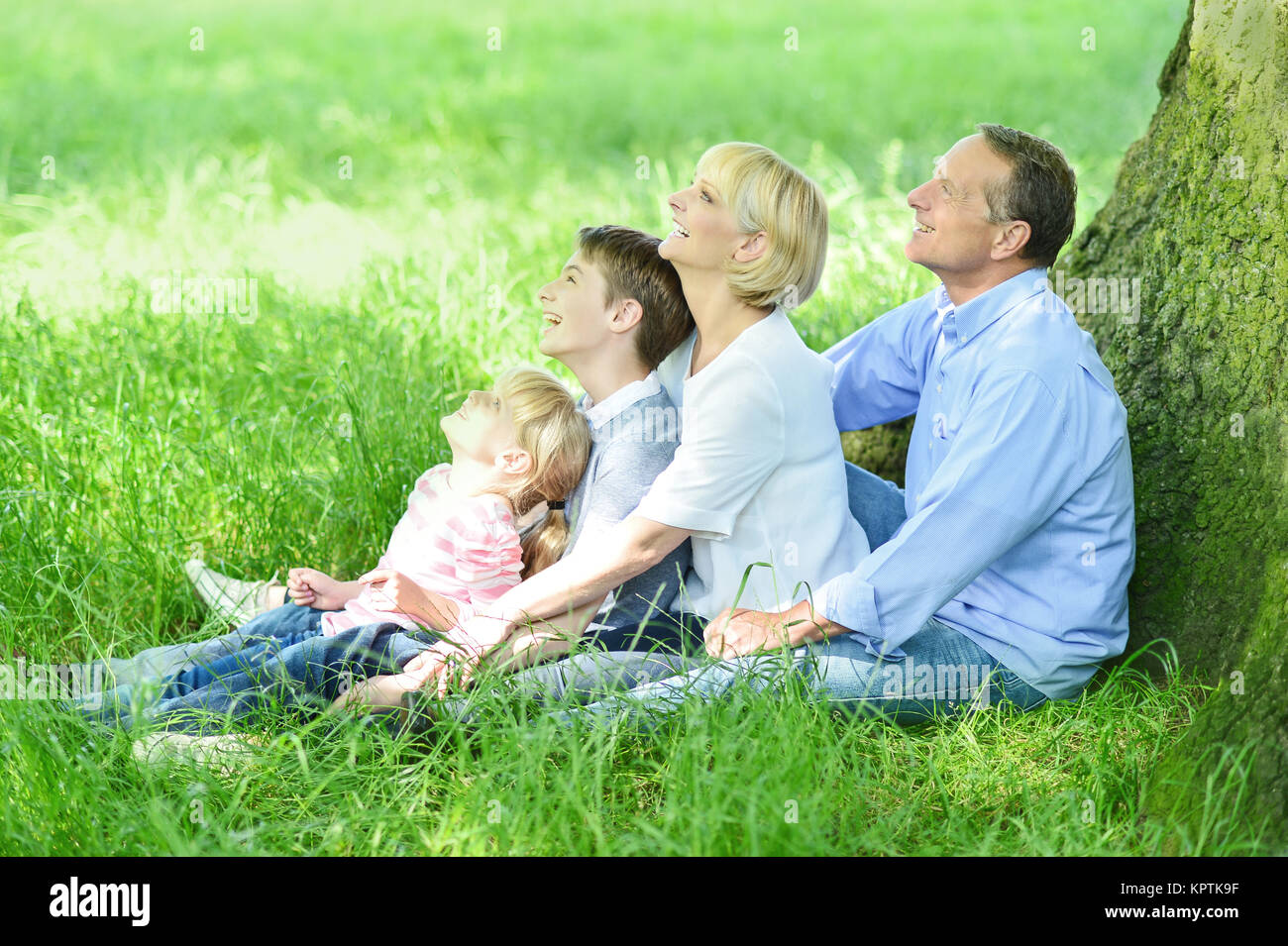 Happy family relaxing under tree Stock Photo - Alamy