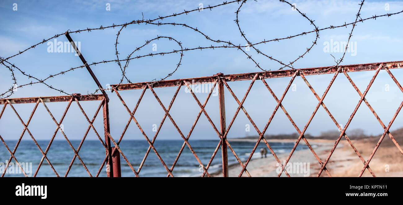 old barbed wire fence on the beach in front of blue water Stock Photo ...
