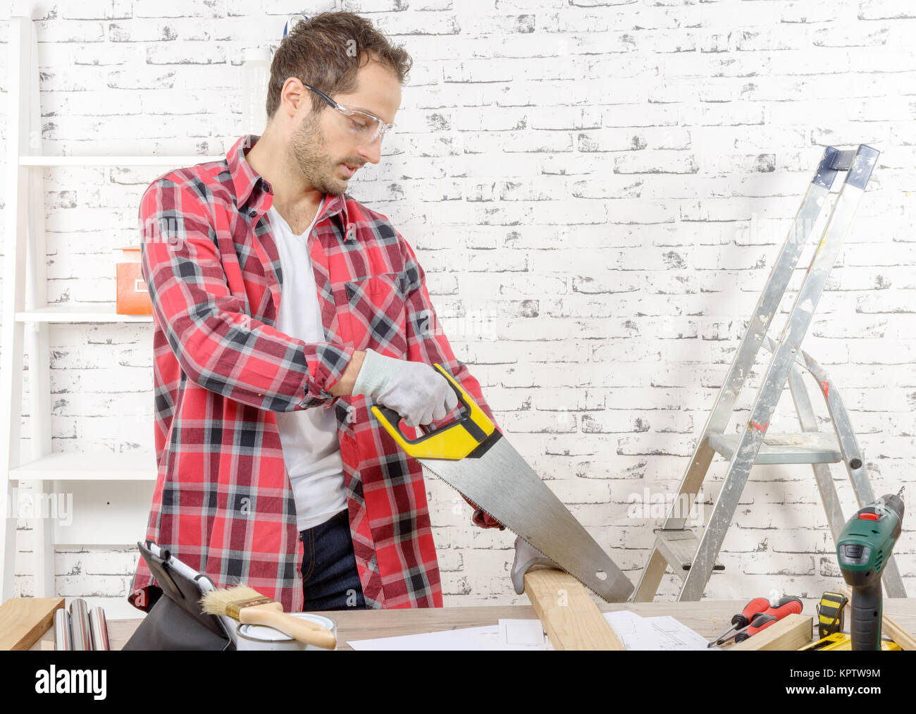 a smiling young man cutting a board with a hand saw Stock Photo - Alamy