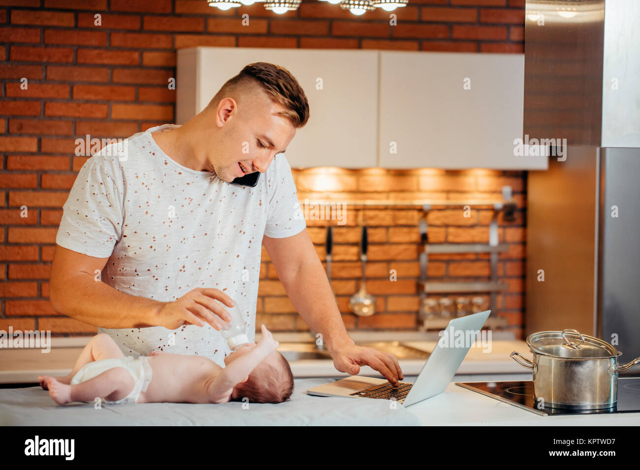 single dad working on laptop computer at home while taking care of his ...