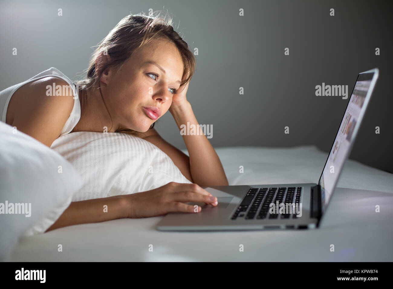 Pretty, young woman using her laptop computer in bed (color toned image ...