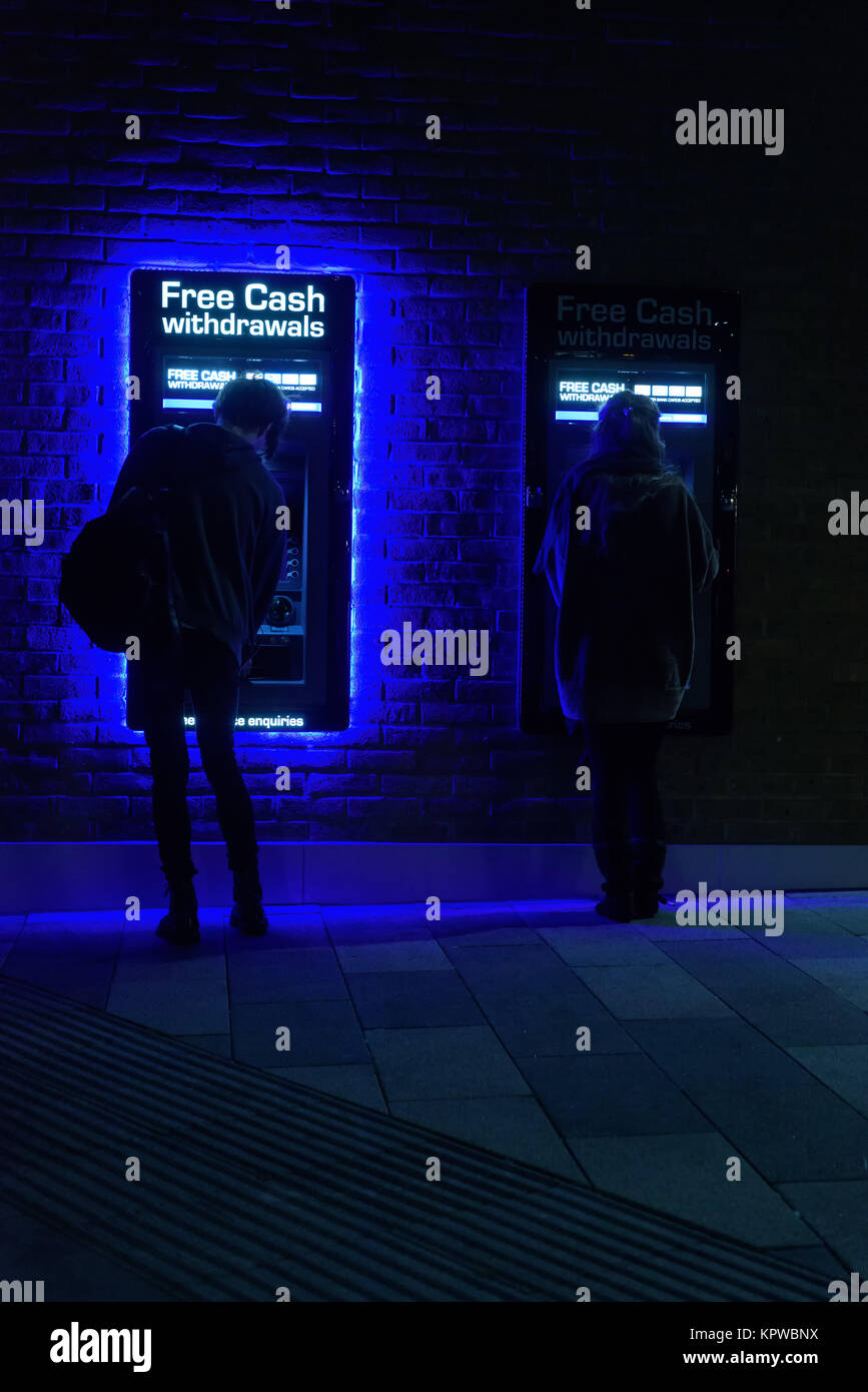 Two people at night using cash machine ATMS illuminated by the money ...