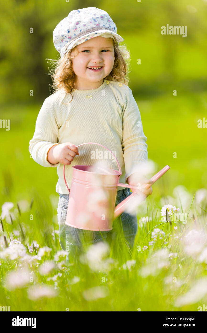 Sweet little toddler watering flowers with a pink water can on a garden ...