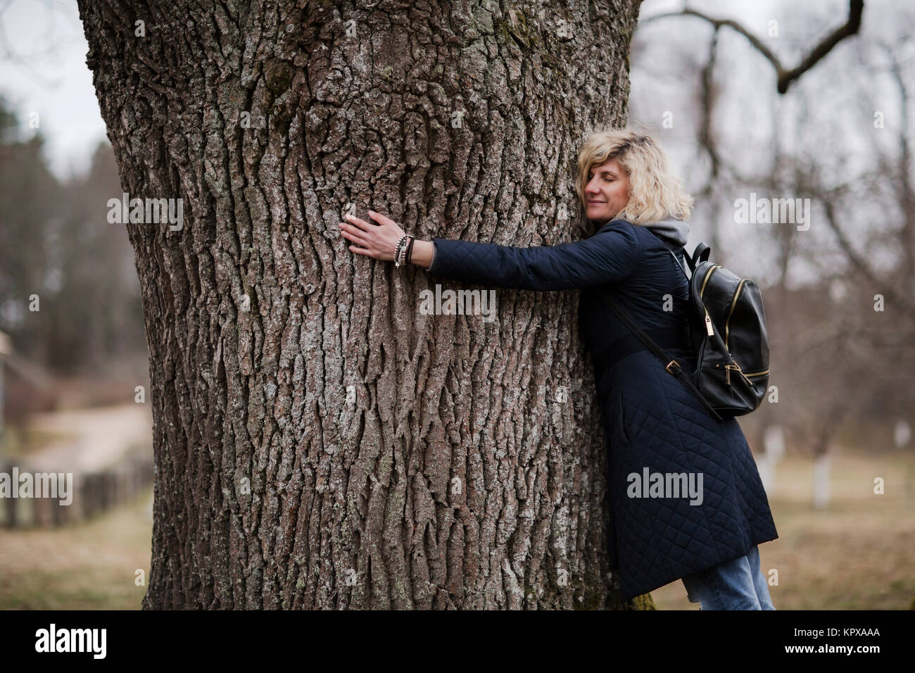 Beautiful blonde girl is hugging tree trunk Stock Photo - Alamy