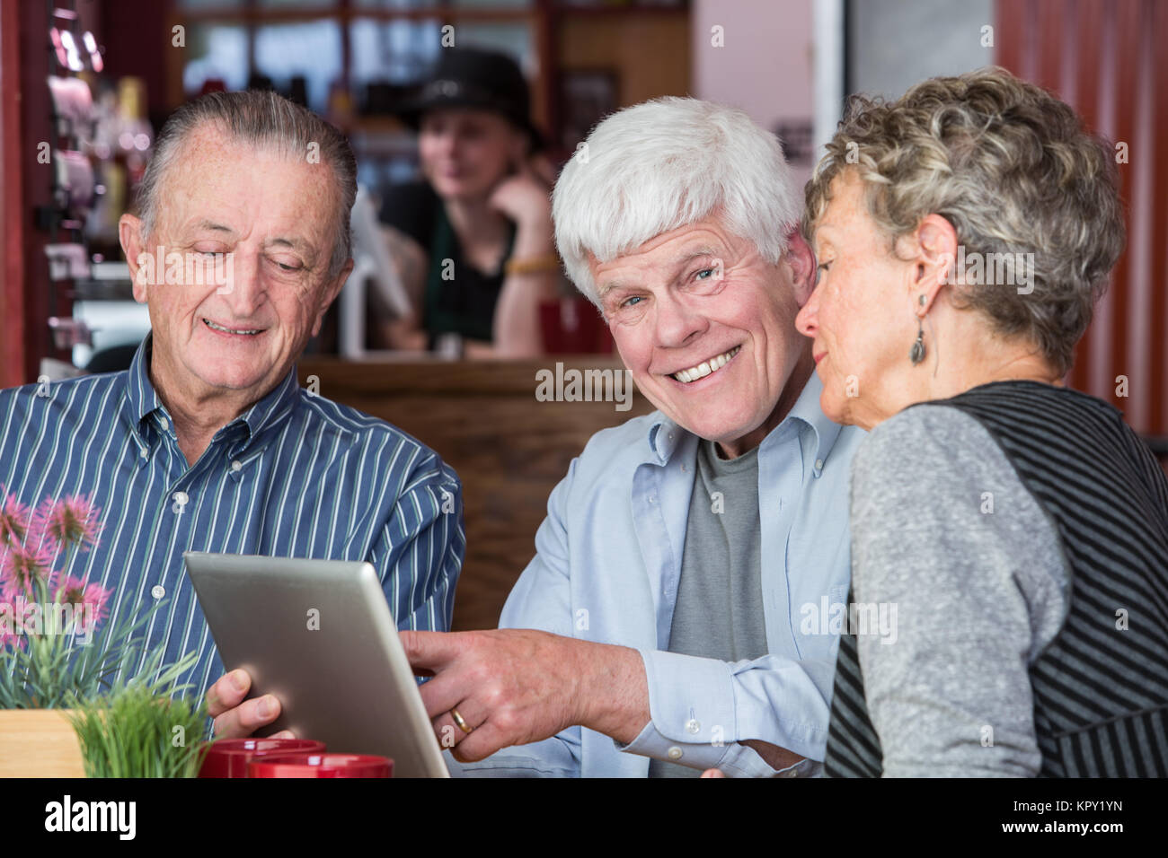 Three senior citizens using tablet computer in bistro Stock Photo - Alamy