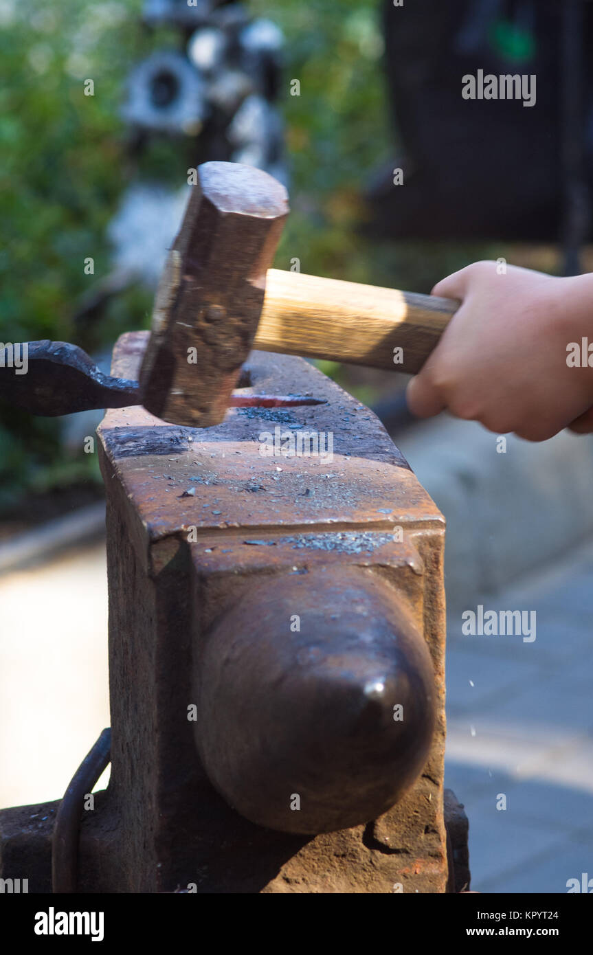 blacksmith performs the forging of hot glowing metal on the anvil ...