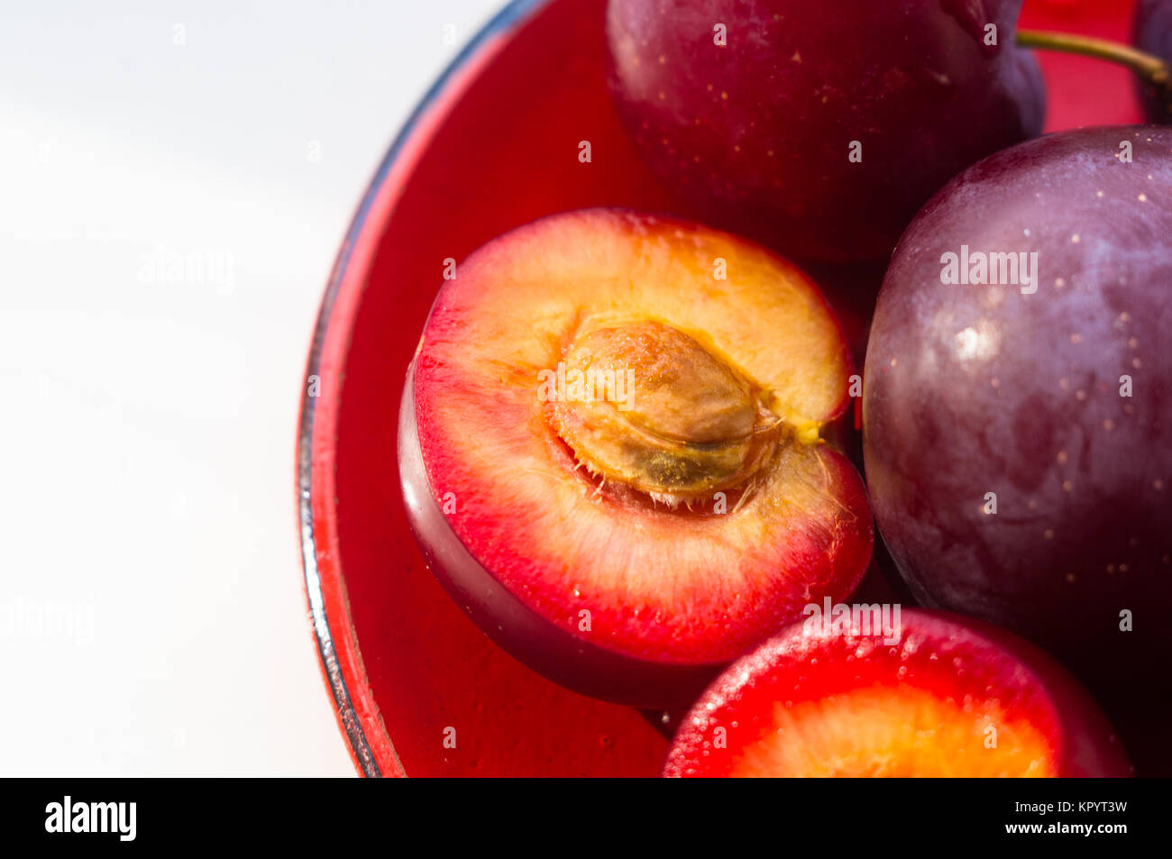 fresh plum fruit with cut plum slices in the red saucer on white ...