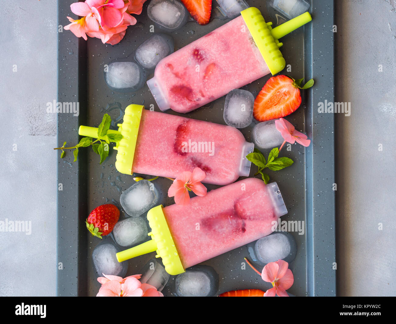 Home made strawberry ice cream popsicles on metall tray with ice cubes ...