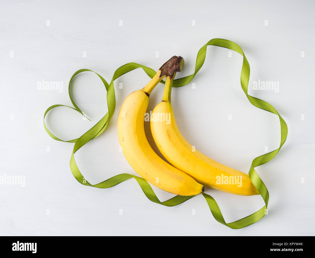 Two bananas with green ribbon frame and heart symbol on white ...