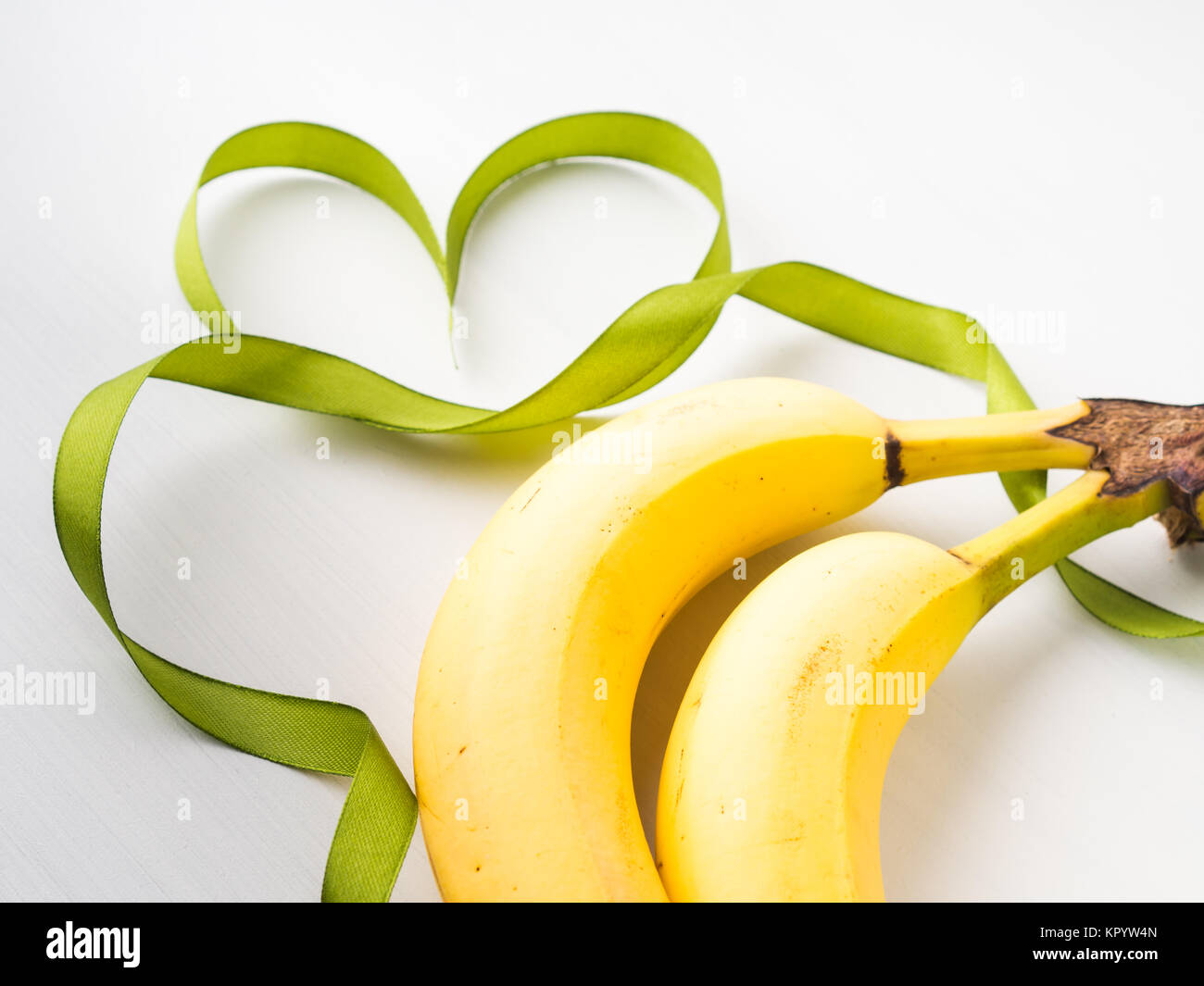 Two bananas with green ribbon frame and heart symbol on white ...
