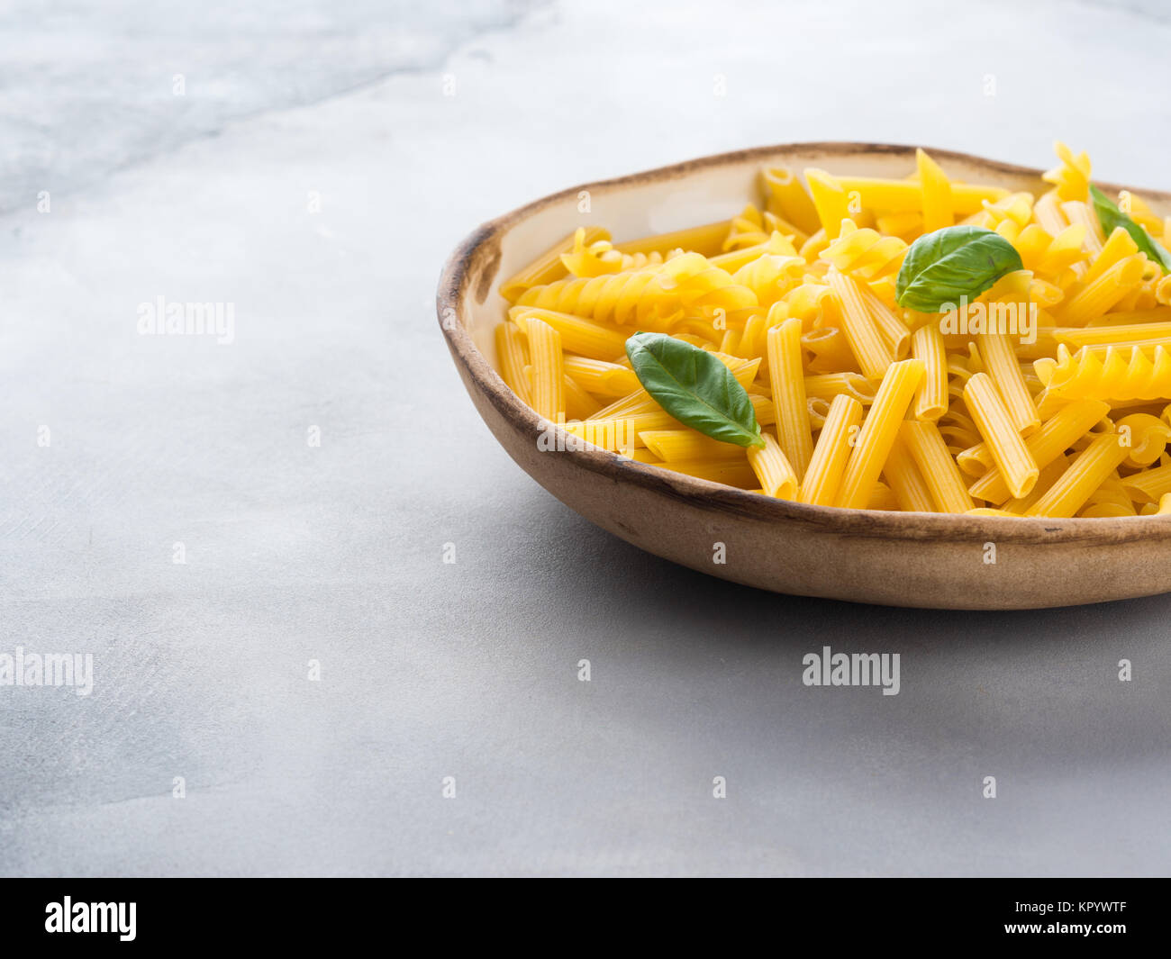 Italian raw short pasta in a dish with basil leaves on gray background ...