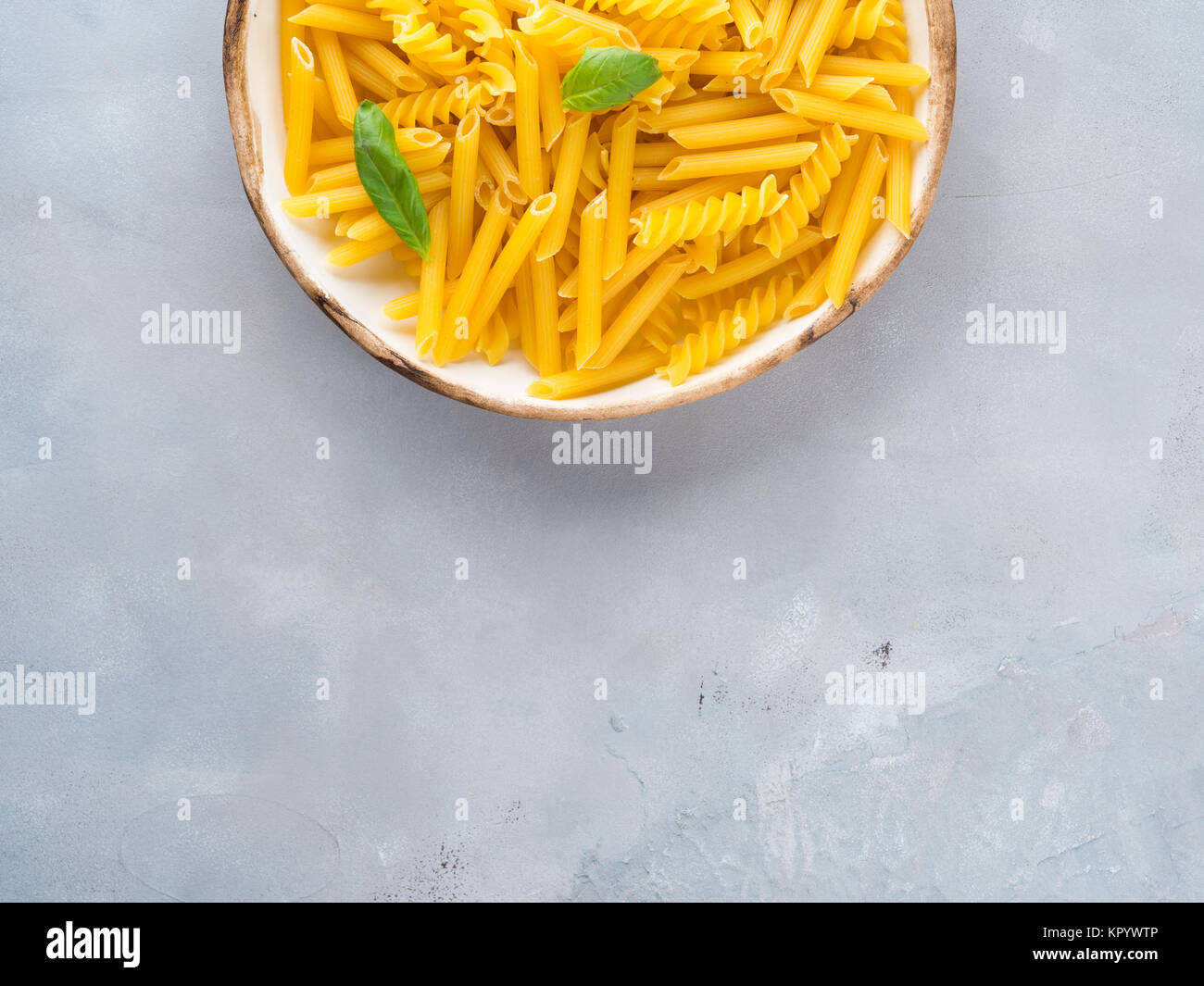 Italian raw short pasta in a dish with basil leaves on gray background ...