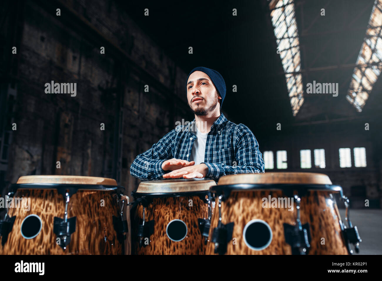 Male drummer plays on wooden drum in big factory shop, front view ...
