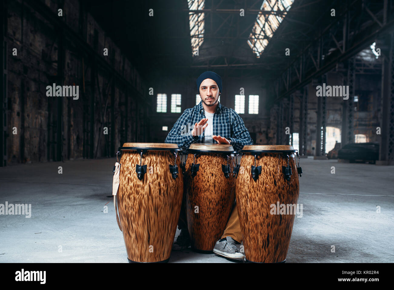 Male drummer plays on wooden drum in big factory shop, front view ...