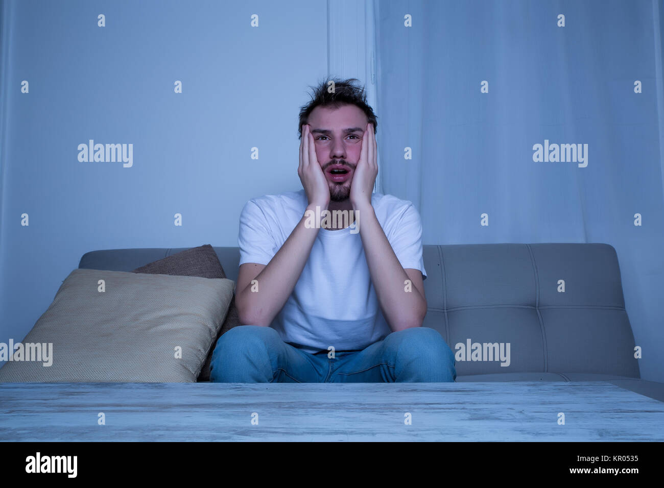 A young man sitting on the sofa in the living room is shocked by a ...