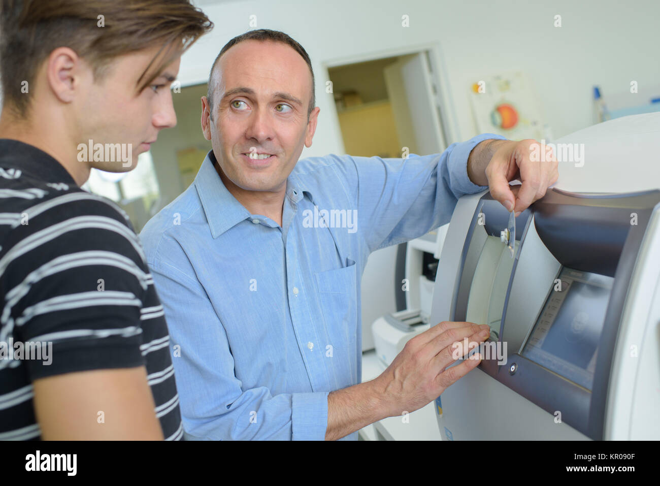 Man showing younger man how to use cash machine Stock Photo - Alamy