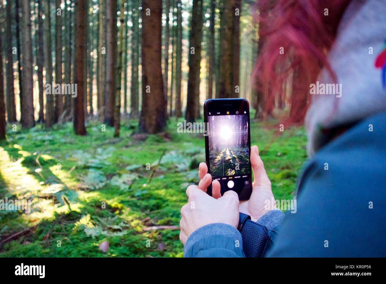 Woman taking a mobile phone photograph of beams of sunlight through ...