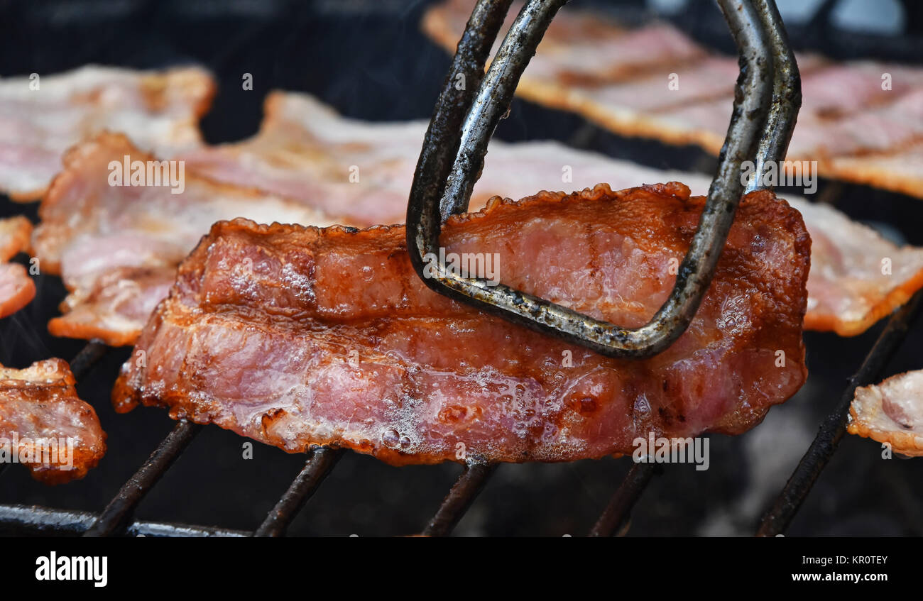 Tongs with bacon slice cooked on bbq grill Stock Photo - Alamy