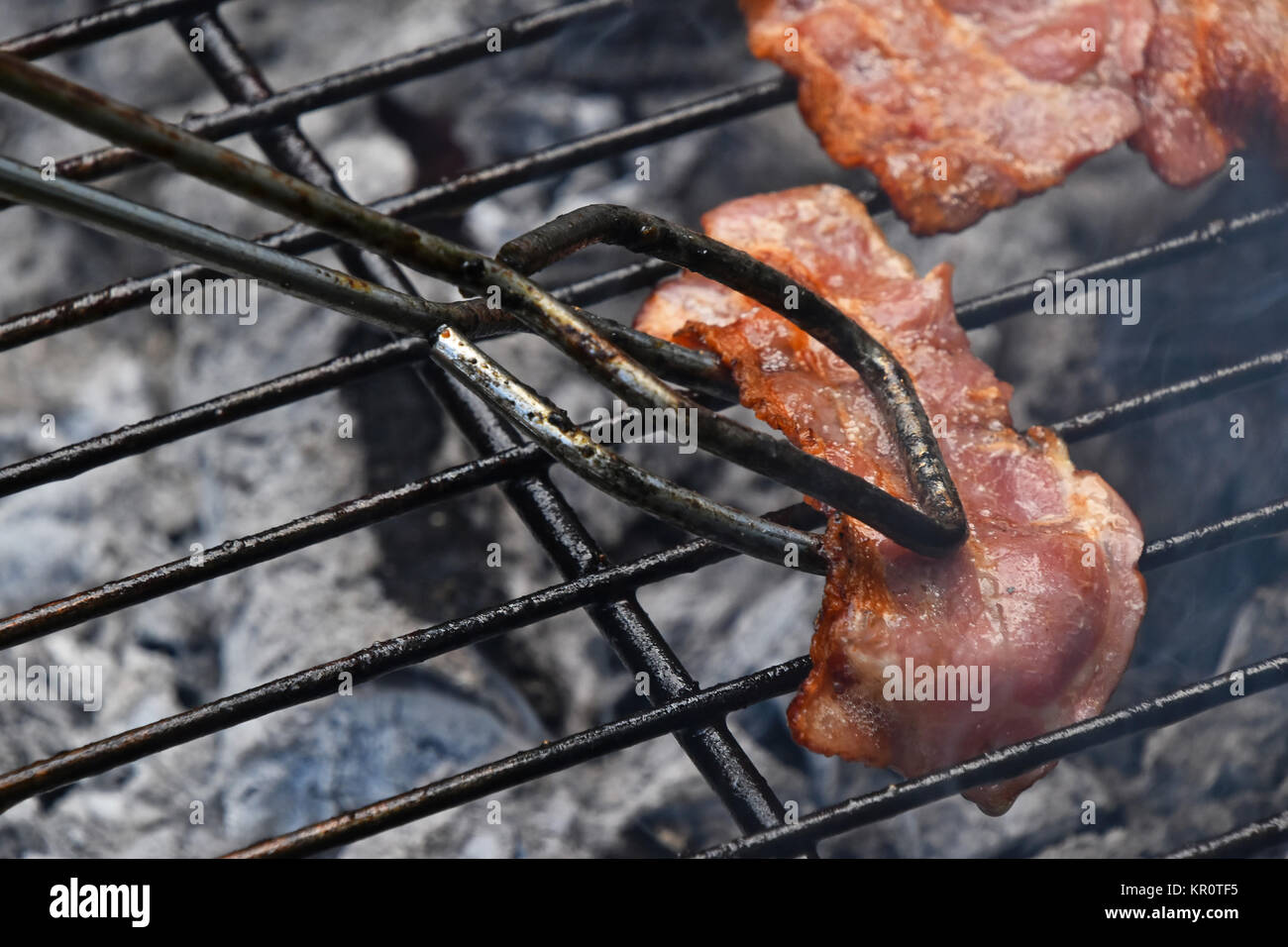 Tongs with bacon slice cooked on bbq grill Stock Photo - Alamy