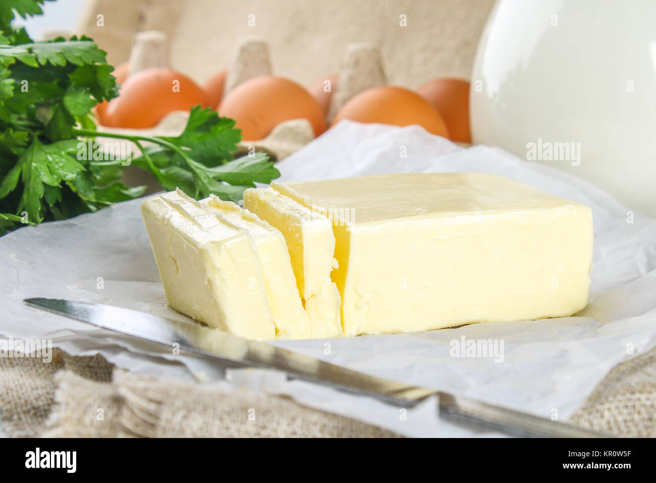A bar of butter is cut into pieces on a wooden board with a knife ...