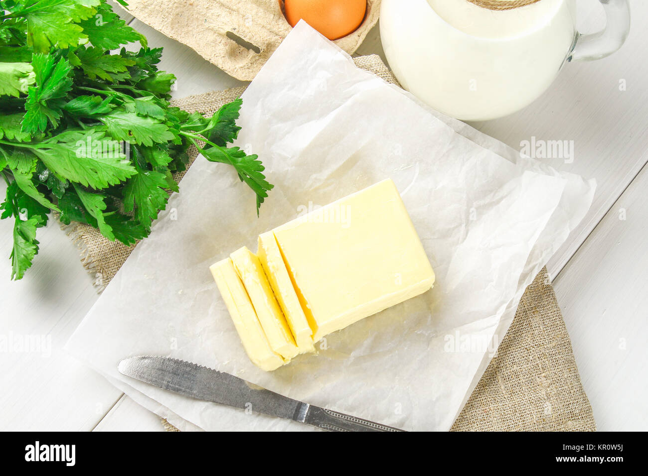 A bar of butter is cut into pieces on a wooden board with a knife ...