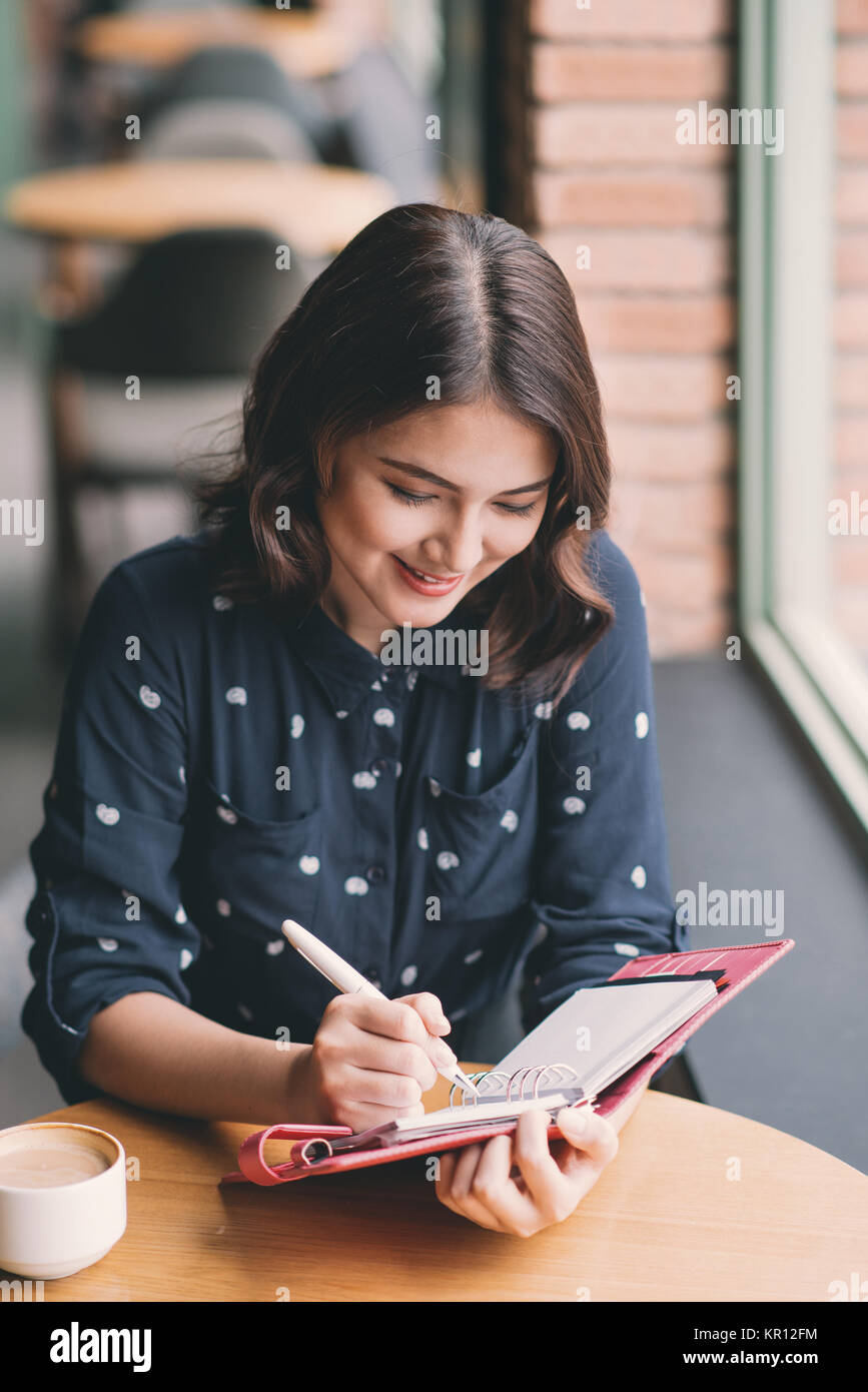 Young beautiful woman in the cafe near the window, thinking and writing ...