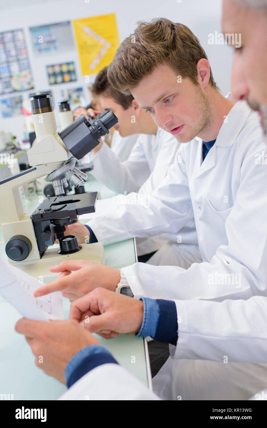 Students in lab using microscopes, reading paperwork Stock Photo - Alamy