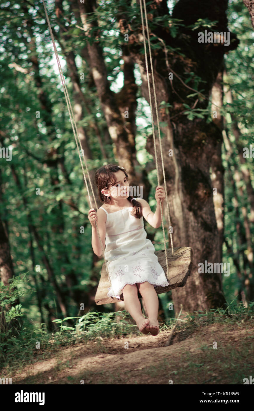 Pretty young girl swinging in the forest on a rope swing. Summer time ...