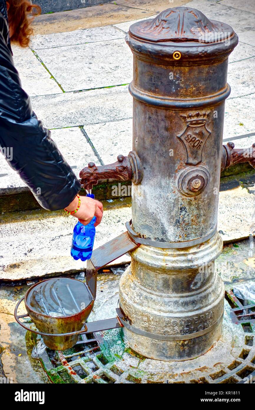 Filling a blue plastic bottle with water at an old drinking fountain in ...