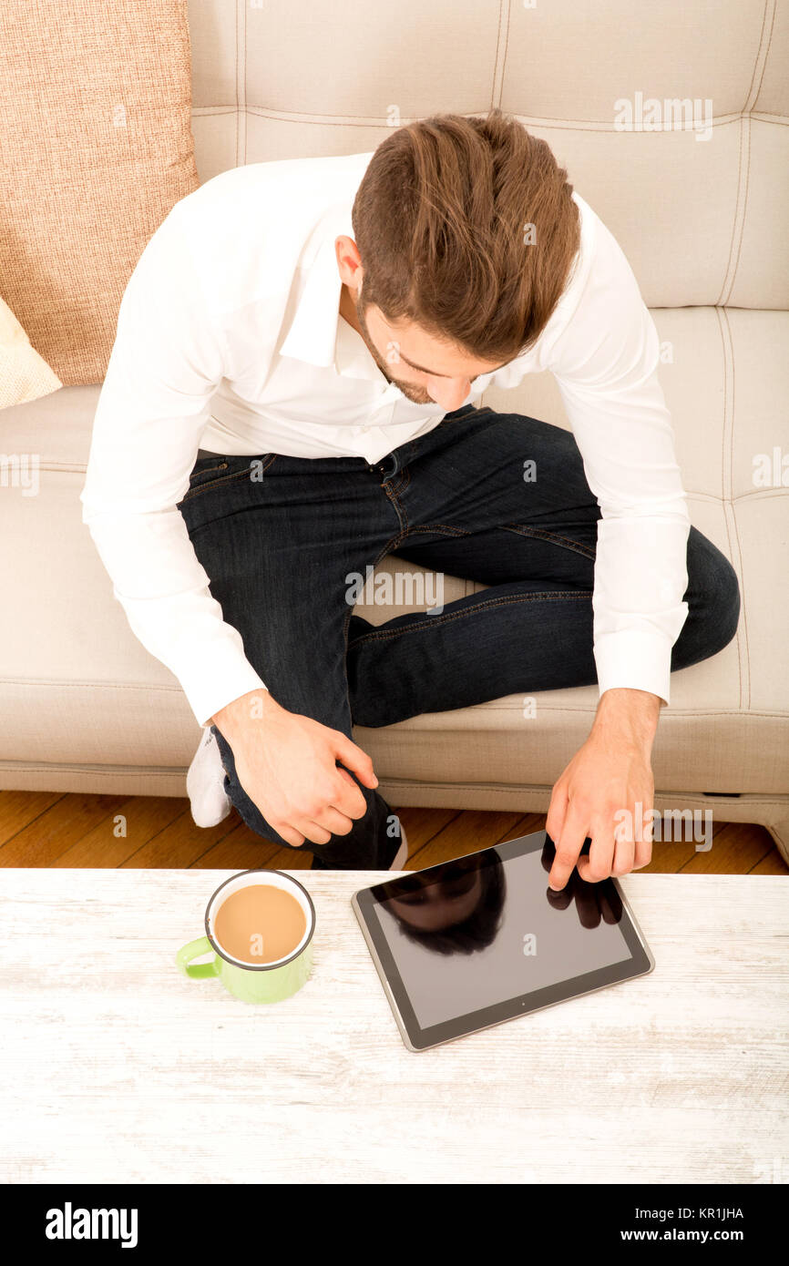 A young adult man sitting on the couch using a tablet Stock Photo - Alamy