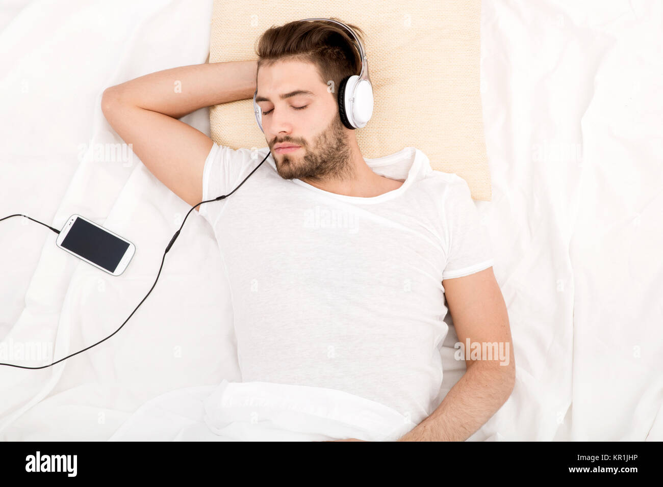 Portrait of a man from above with headphones and smartphone in bed ...