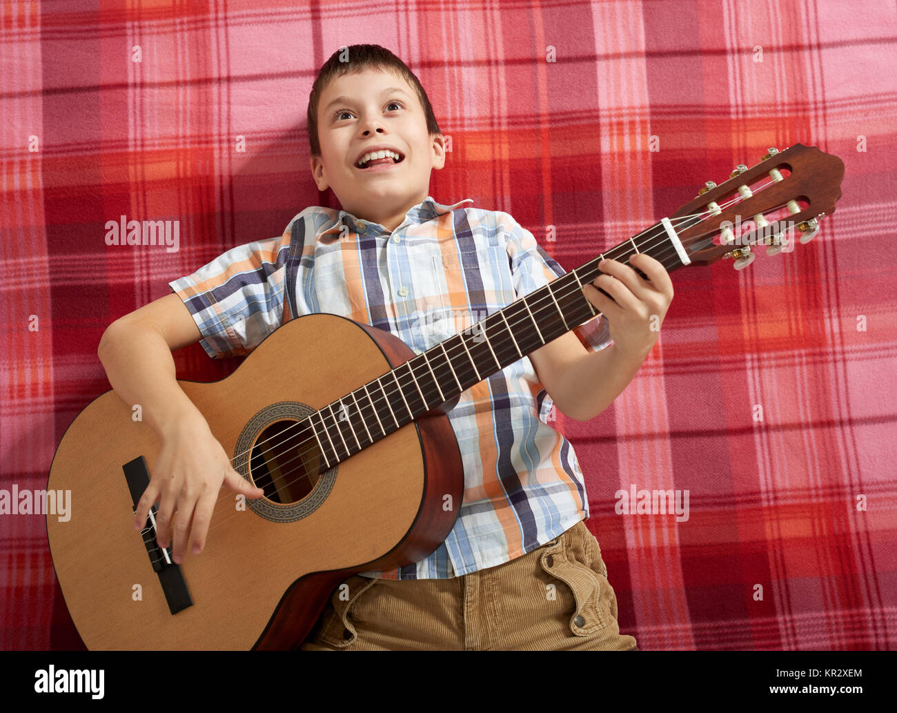 boy playing music on guitar, lies on a red checkered blanket, top view ...