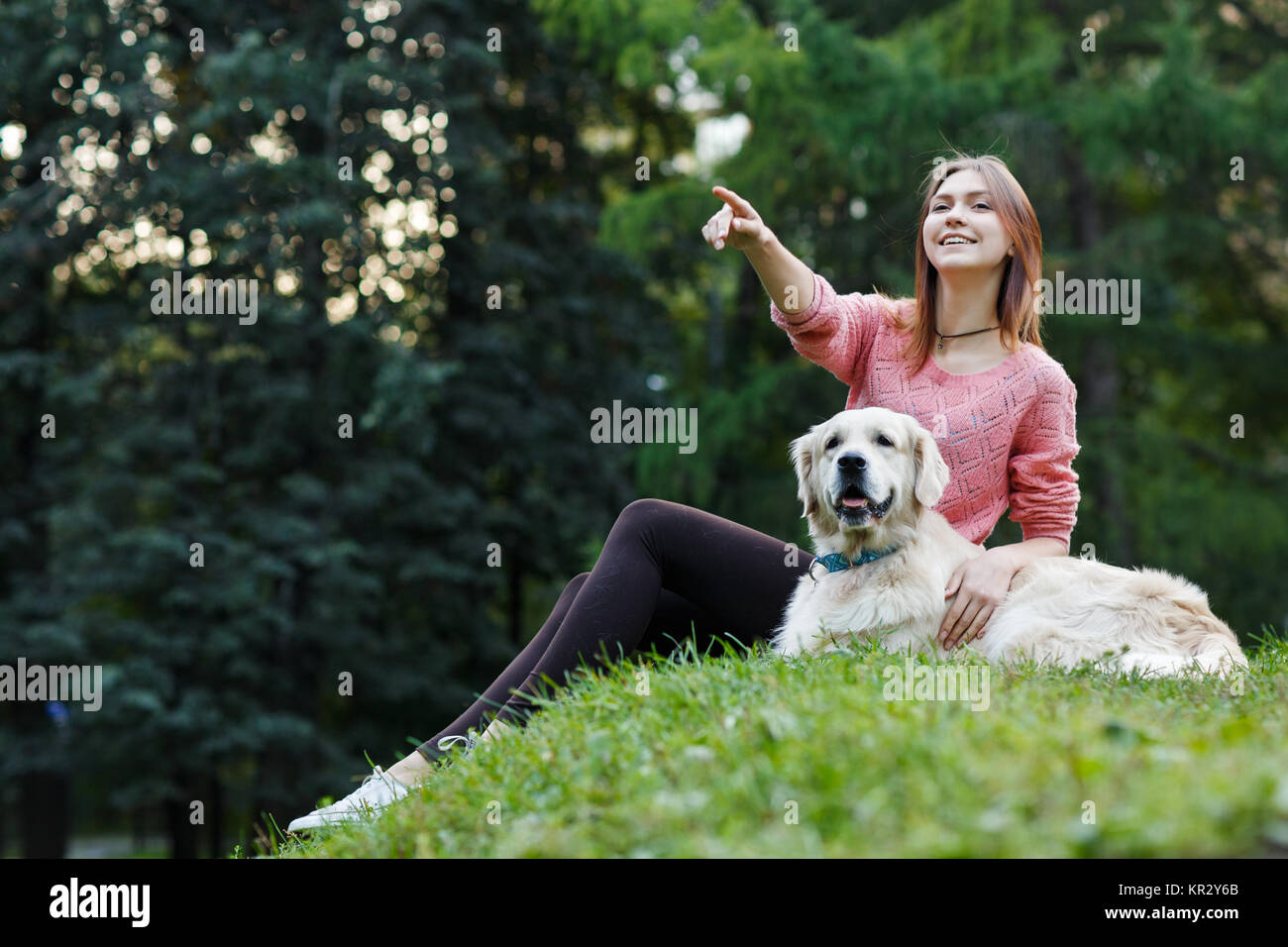 Image from below of woman pointing forward next to dog on green lawn ...