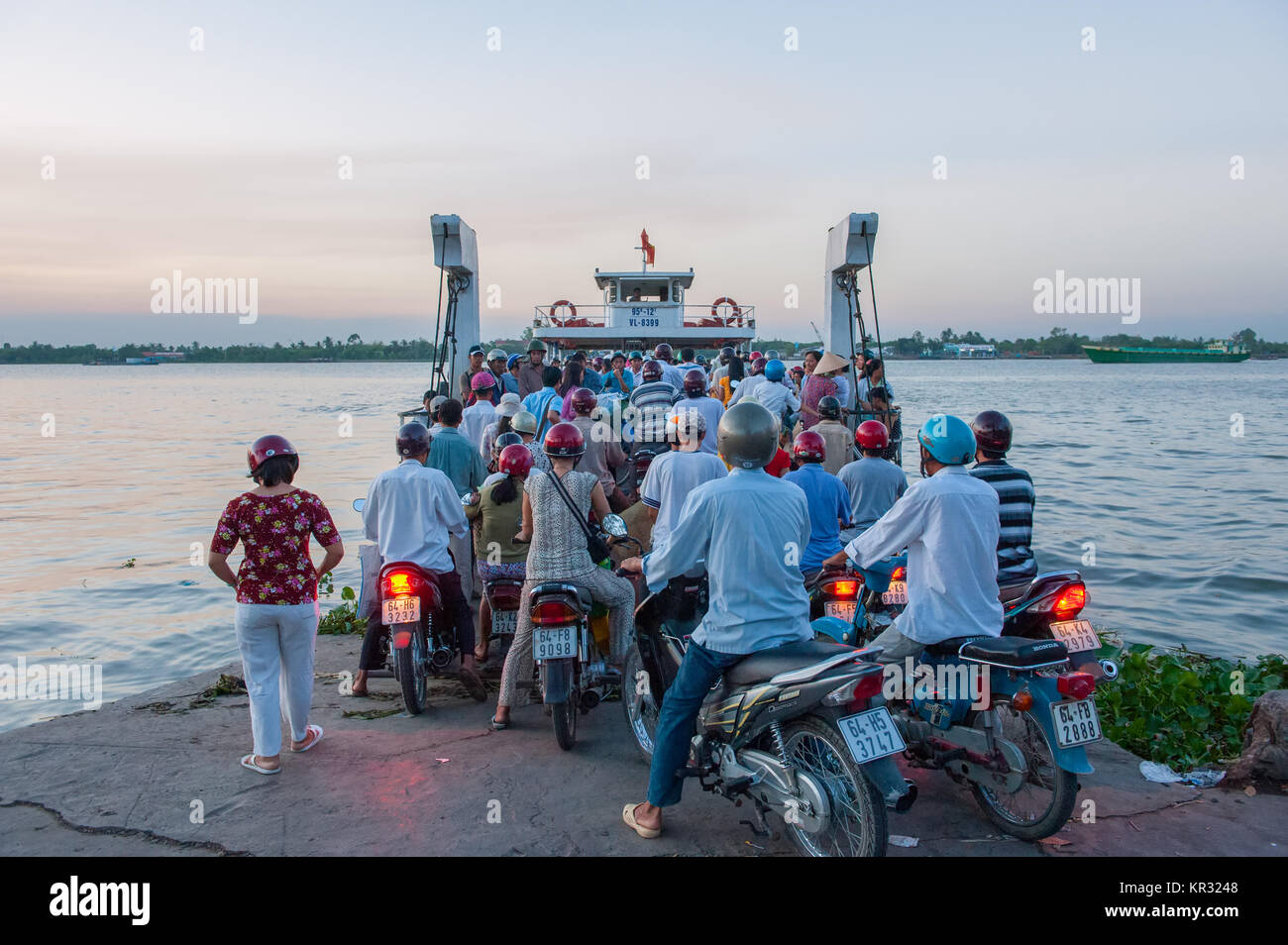 Crowd of bikers trying to access an evening ferry across the Mekong ...