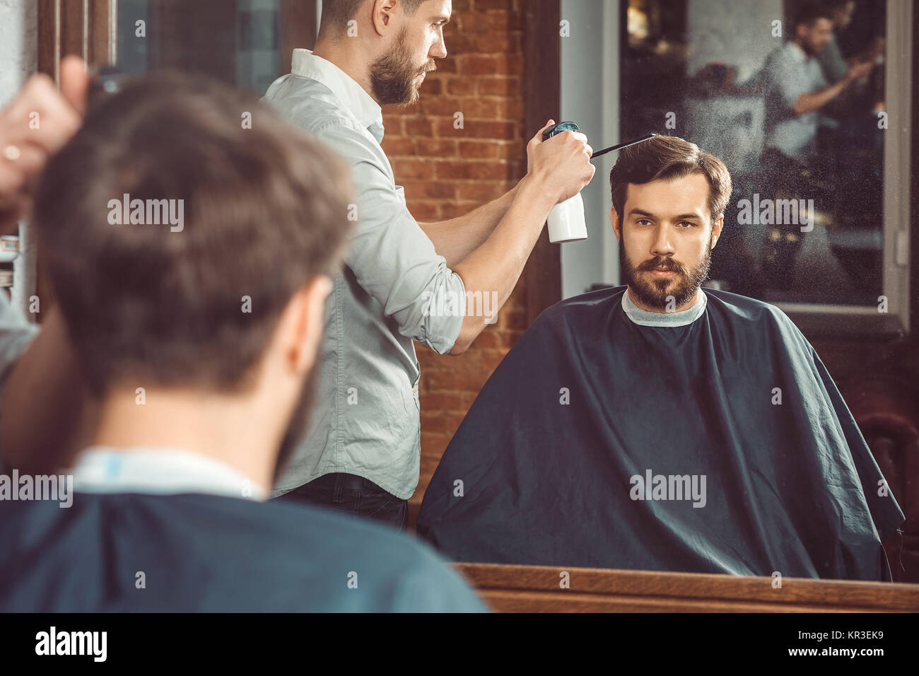 Young handsome barber making haircut of attractive man in barbershop ...